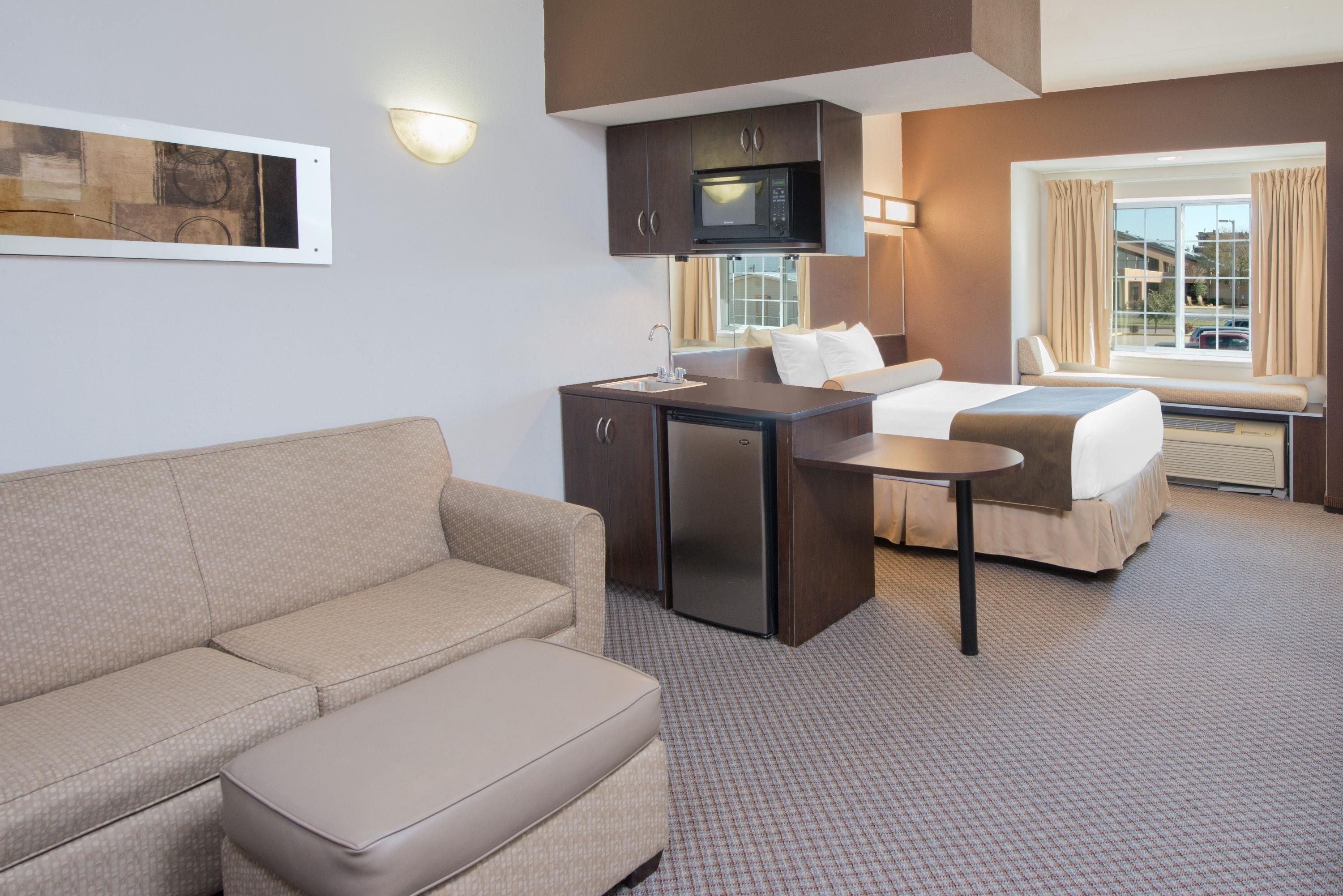 Quarto de hotel com cama, escrivaninha, sofá, televisão e janela com cortinas.