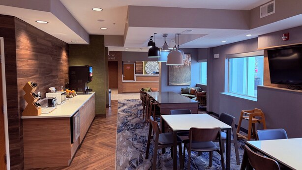Uma área de jantar de hotel moderna, com uma ilha central, assentos e uma TV fixada na parede.