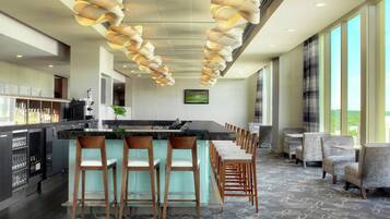 Uma área de bar moderna com um balcão comprido, banquetas e uma tela grande.