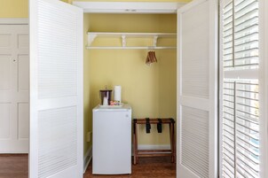 Uma lavanderia compacta com um frigorífico branco, uma pequena mesa com roupa pendurada e uma janela com persianas.