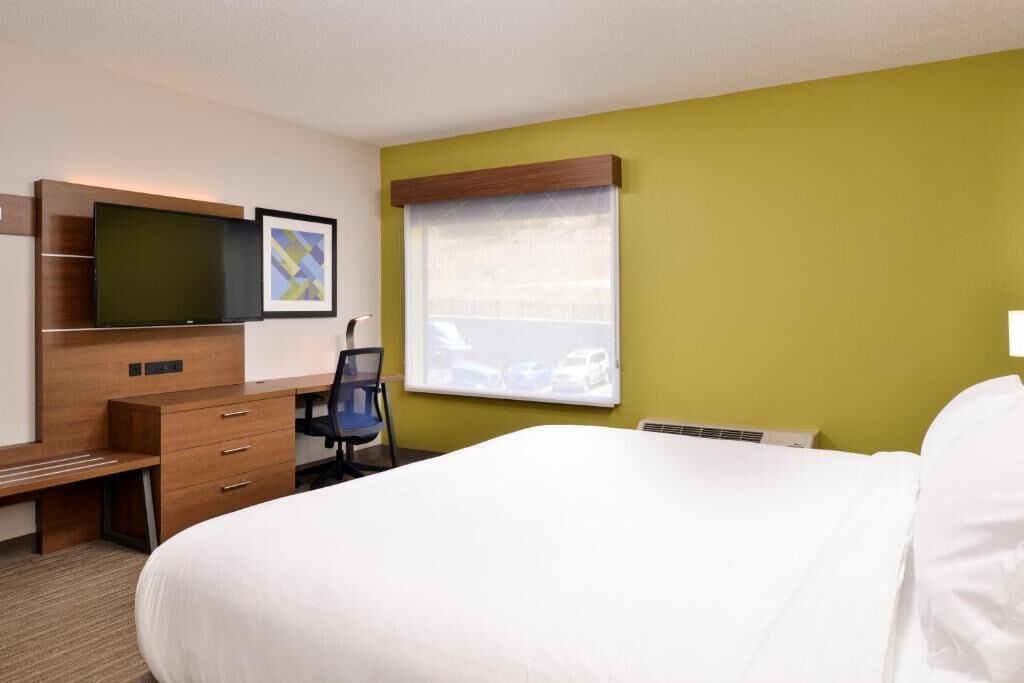 Quarto de hotel com cama, escrivaninha, cadeira, televisão e janela com vista para carros.