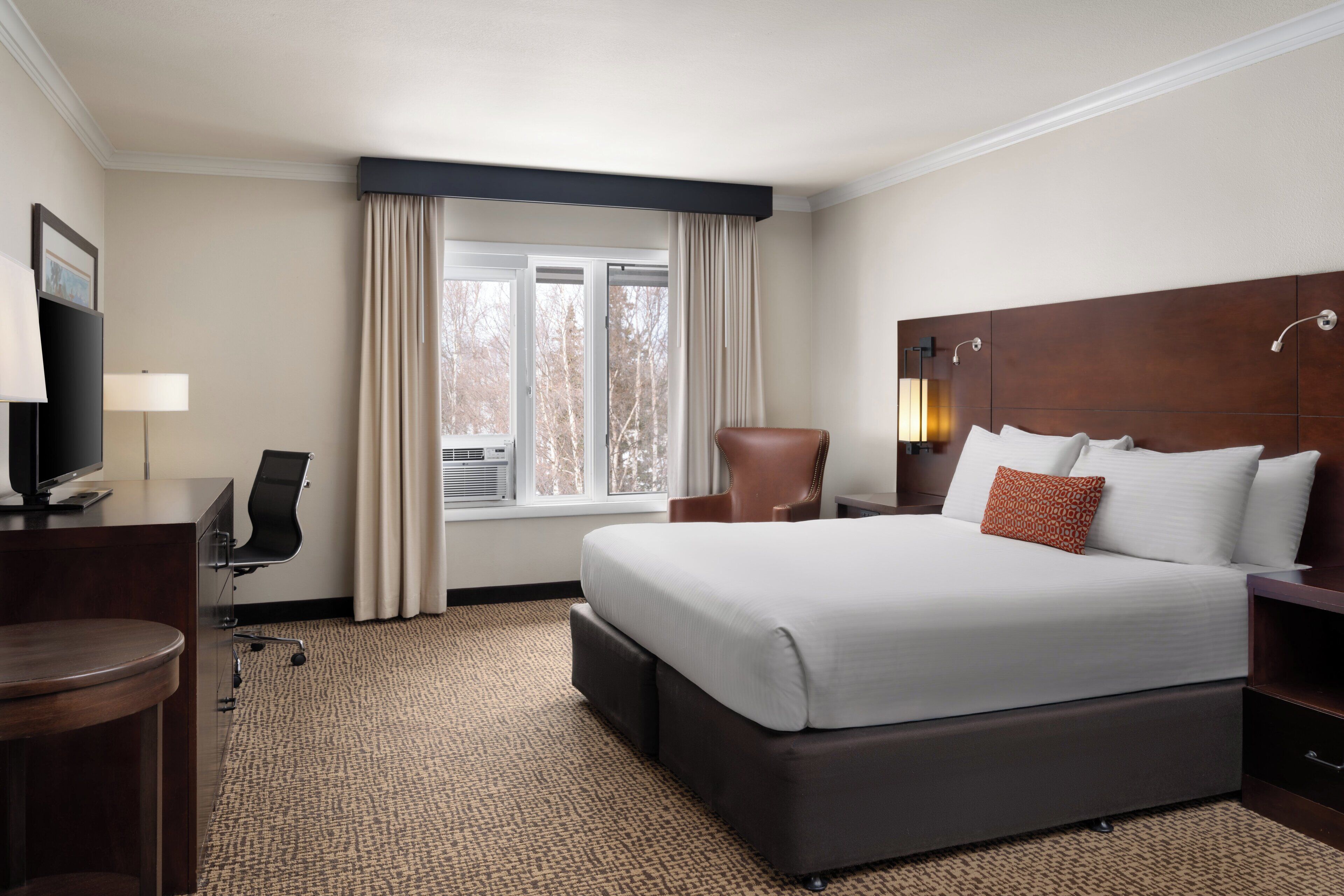 Quarto de hotel com uma cama grande, uma mesa, uma cadeira, uma televisão e uma janela com cortinas.