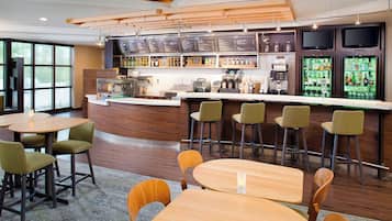 Uma área de bar moderna com mesas e cadeiras de madeira, um balcão com menu e um bar abastecido com garrafas.