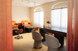 Quarto de hotel moderno com escrivaninha de madeira escura, duas cadeiras de escritório, um sofá e um espelho grande.