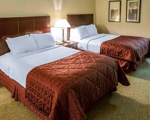Duas camas de casal com roupa de cama branca e colchas estampadas em vermelho num quarto de hotel.