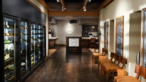 Interior de restaurante com um balcão comprido, cadeiras de madeira e uma seleção de garrafas de vinho.