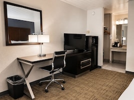 Quarto de hotel com escrivaninha, cadeira, televisão, micro-ondas e uma pequena cozinha.