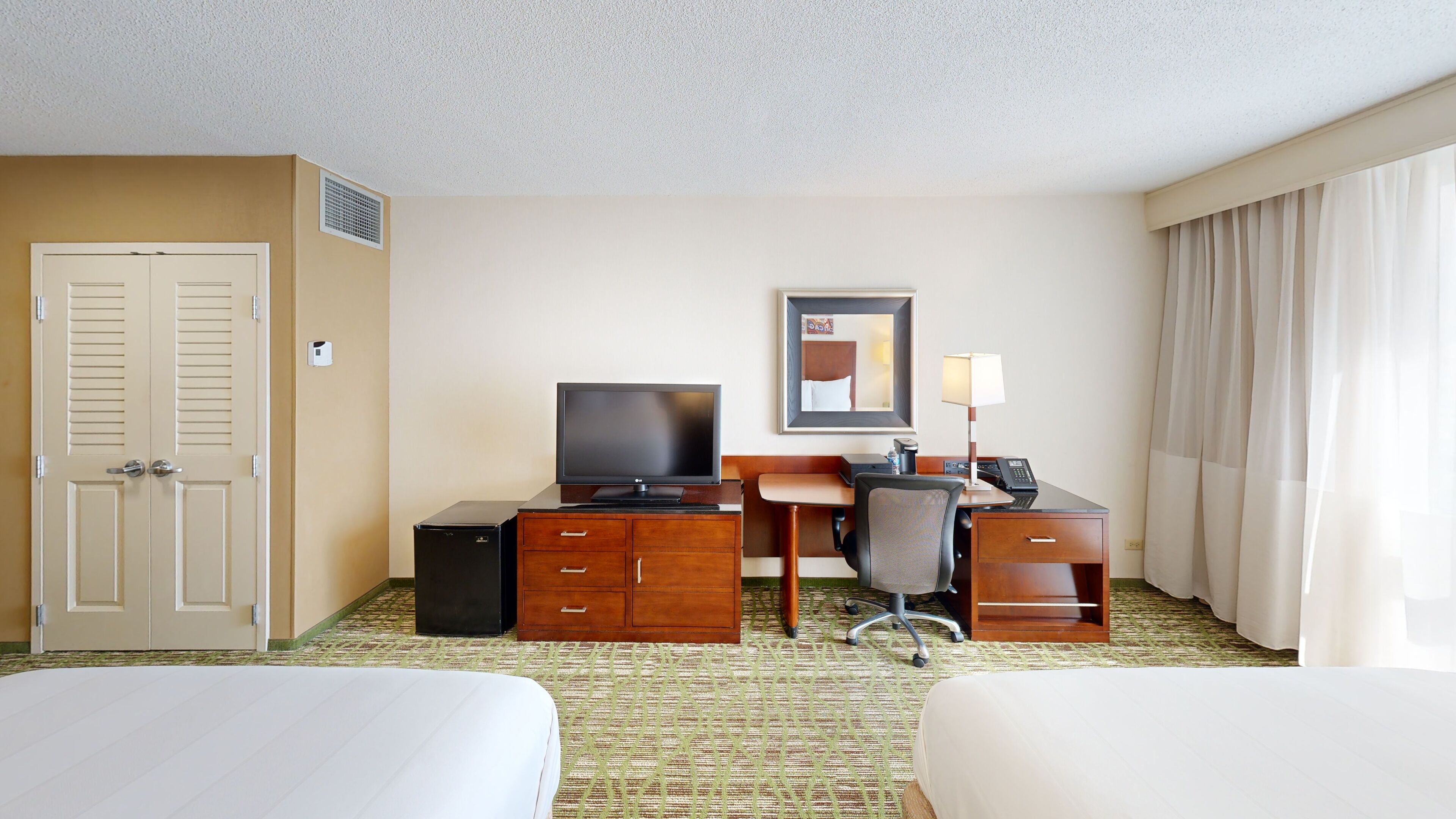 Quarto de hotel com duas camas, uma escrivaninha com computador, televisão e um pequeno frigorífico.