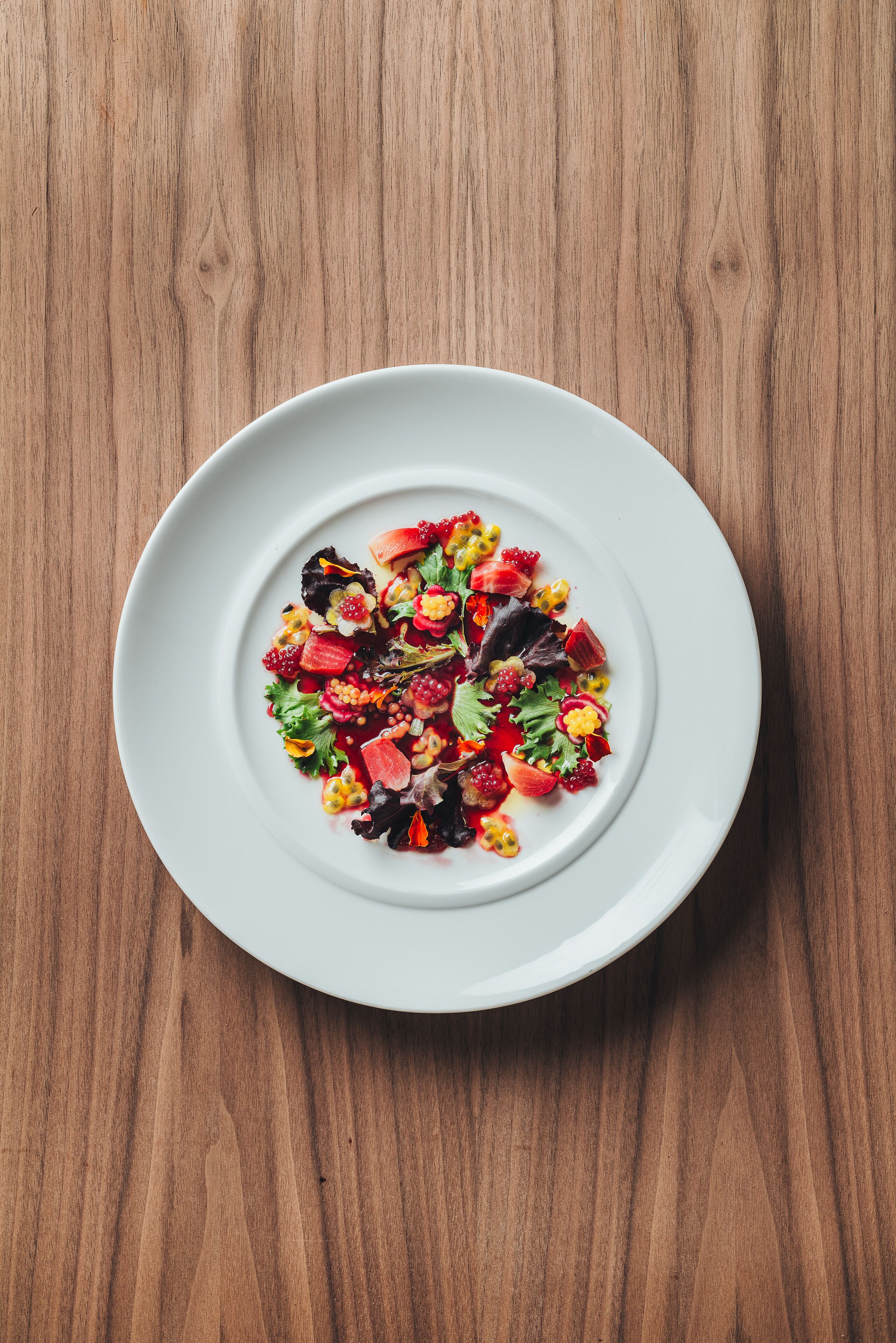 Uma salada colorida num prato branco sobre uma mesa de madeira.