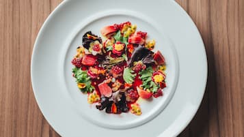 Uma salada colorida num prato branco sobre uma mesa de madeira.
