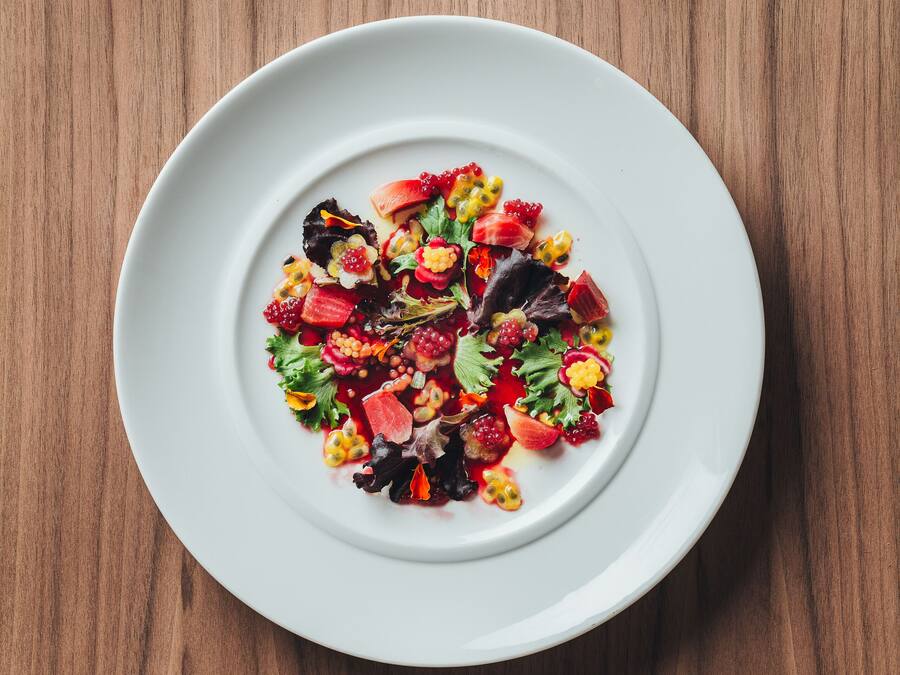 Uma salada colorida num prato branco sobre uma mesa de madeira.