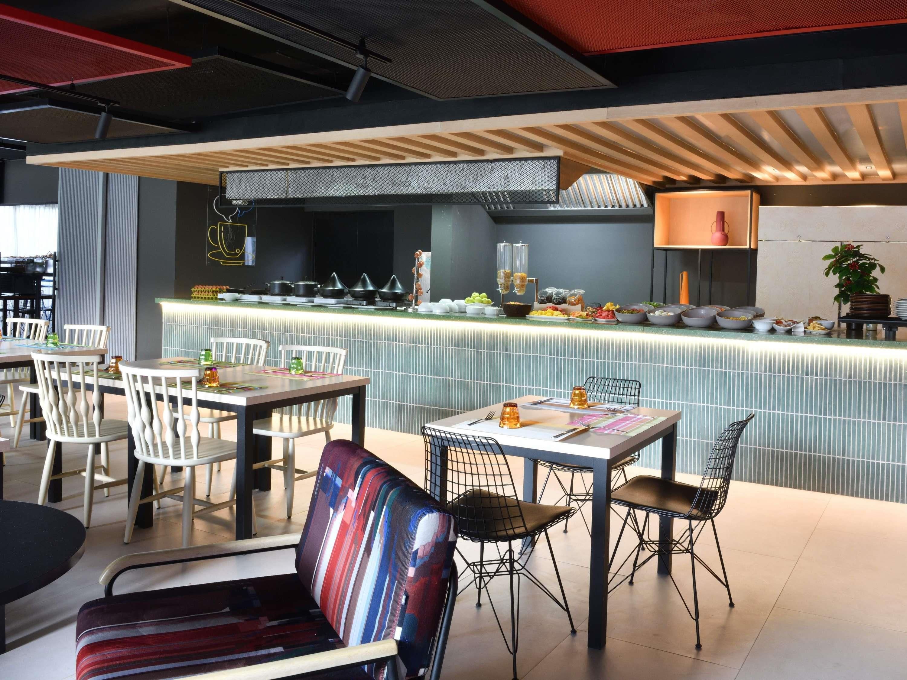 Um restaurante moderno com área de bar, arranjos de assento e cozinha visível ao fundo.