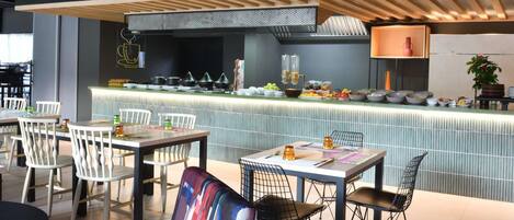 Um restaurante moderno com área de bar, arranjos de assento e cozinha visível ao fundo.
