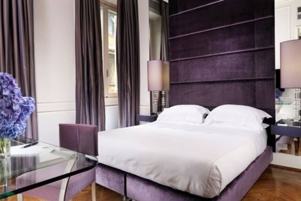Quarto de hotel com uma cama, uma mesa de vidro, uma cadeira e um vaso de flores.