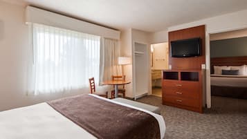 Quarto de hotel com cama, escrivaninha, cadeira, televisão e guarda-roupa.