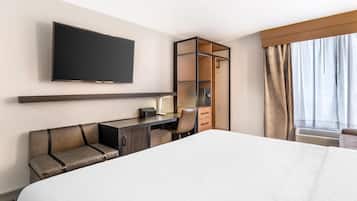 Quarto de hotel com uma cama grande, uma escrivaninha com cadeira, televisão fixada na parede e um guarda-roupa.