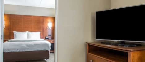 Quarto de hotel com uma cama, uma televisão sobre um suporte de madeira e uma porta que dá para outro cômodo.