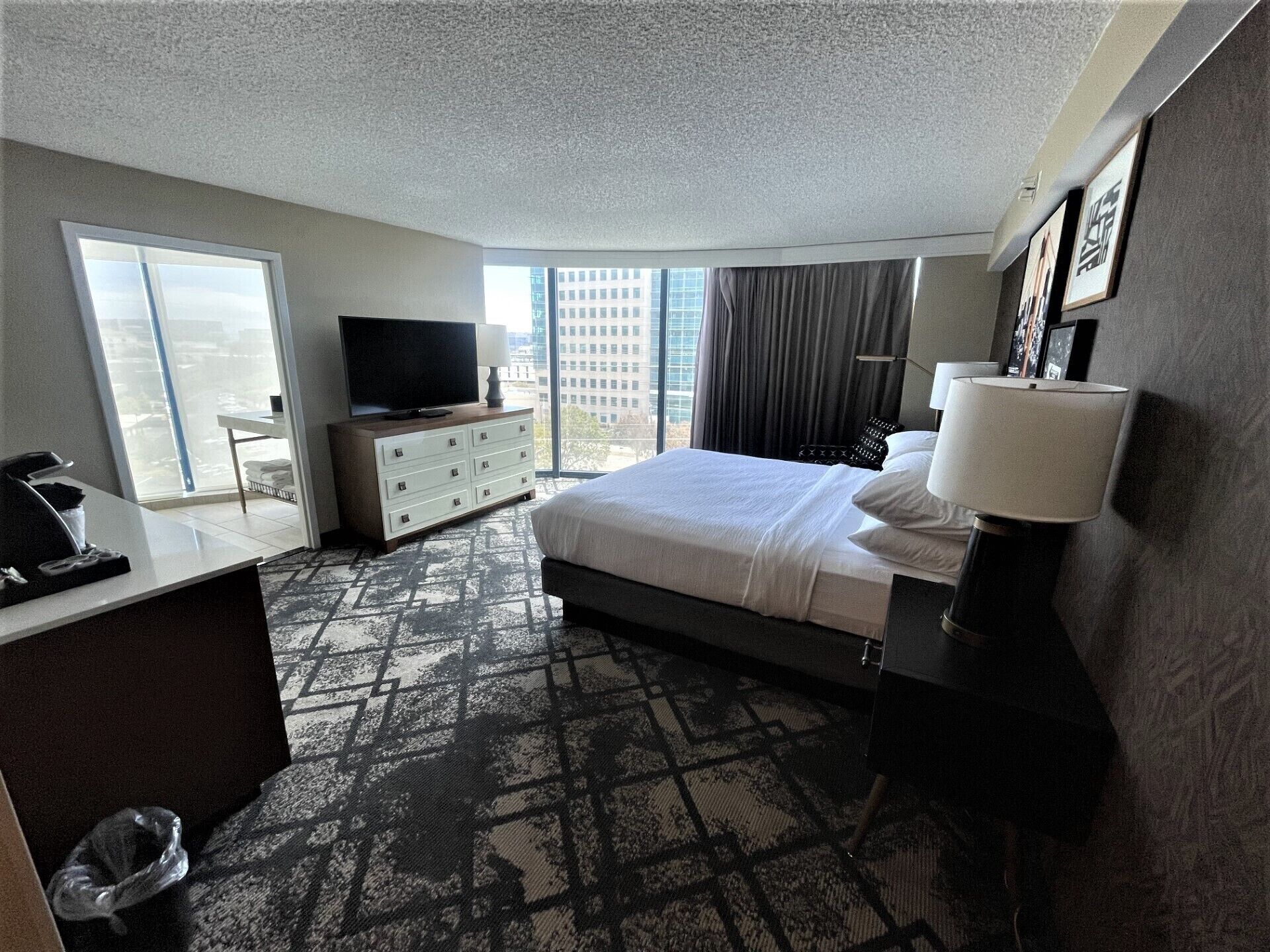 Quarto de hotel com uma cama, televisão, escrivaninha, cômoda e vista para a cidade.