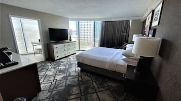 Quarto de hotel com uma cama, televisão, escrivaninha, cômoda e vista para a cidade.