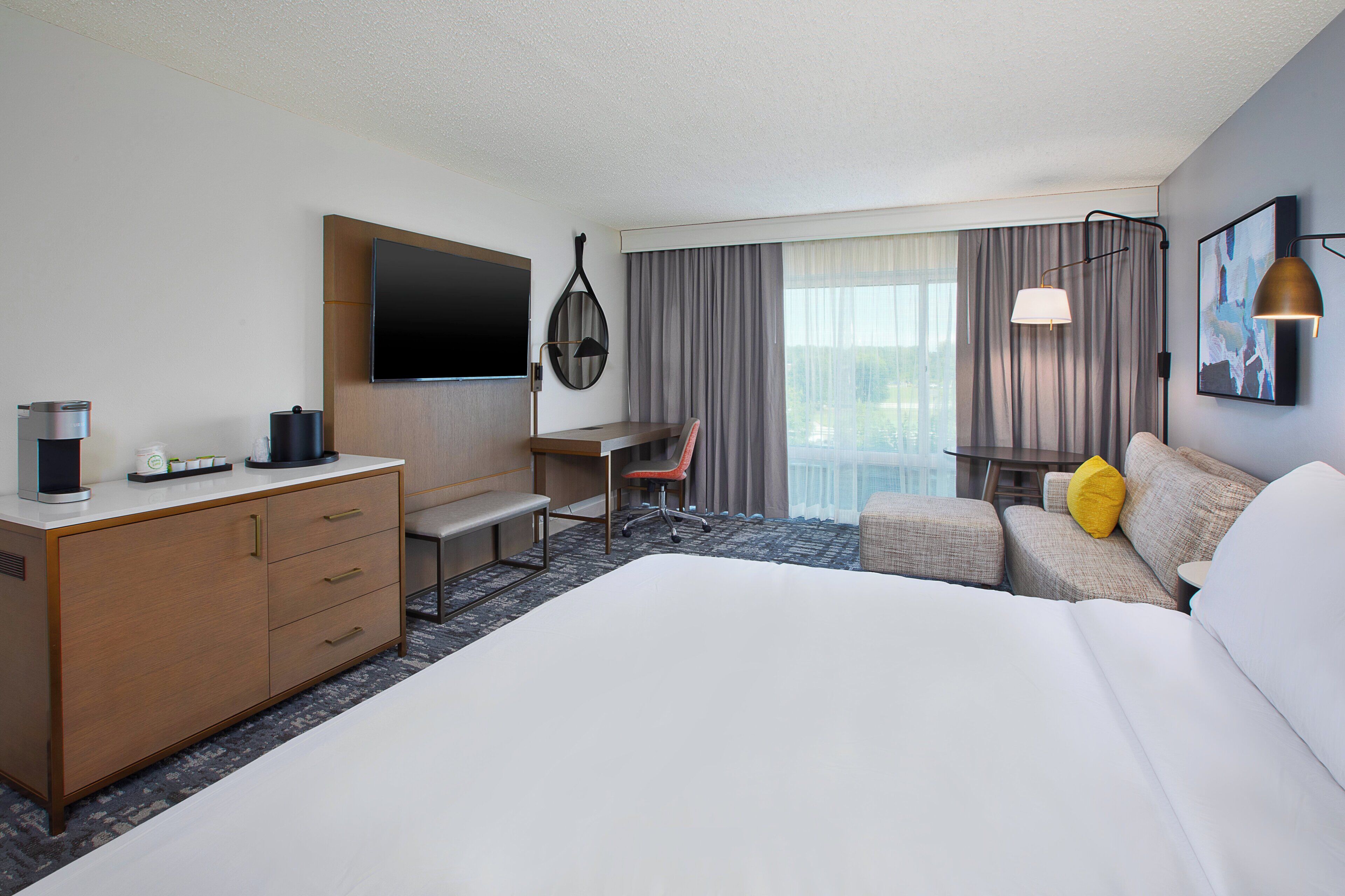 Quarto de hotel com uma cama grande, uma escrivaninha com cadeira, televisão e máquina de café.
