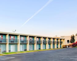 Um motel com uma fileira de quartos, cada um com varanda e pequeno jardim frontal.