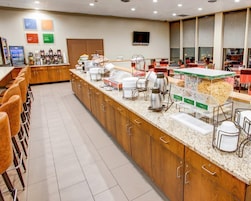 Uma área de pequeno-almoço de hotel com um balcão comprido, cadeiras e uma estação de café.