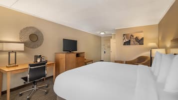 Quarto de hotel com uma cama grande, uma mesa com cadeira, televisão e cafeteira.