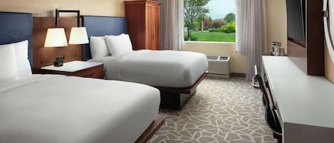 Quarto de hotel com duas camas, uma mesa de escritório, televisão e vista para o exterior.