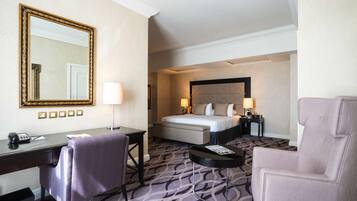 Quarto de hotel com cama, escrivaninha, cadeira e um espelho grande.