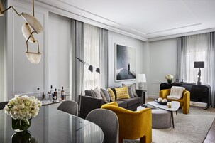 Uma sala de estar moderna com uma mesa de centro de vidro, um sofá com almofadas amarelas e cinzas, um piano preto e uma moldura grande com uma imagem na parede.