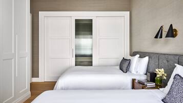 Quarto com duas camas, guarda-roupa, mesa de cabeceira com abajur e vista através de uma porta.