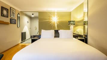 Quarto de hotel com uma cama grande, mesas de cabeceira, um espelho e quadros nas paredes.