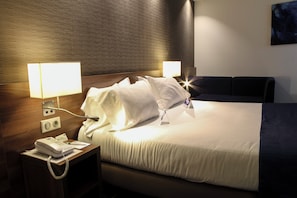 Quarto de hotel com uma cama, abajures, telefone e luminária na parede.