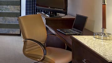 Quarto de hotel com escrivaninha, um laptop, uma cadeira, abajur e vista para montanhas pela janela.