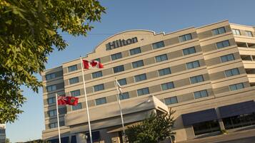 Um hotel com vários andares, um letreiro grande com a inscrição "Hilton", várias janelas e duas bandeiras.