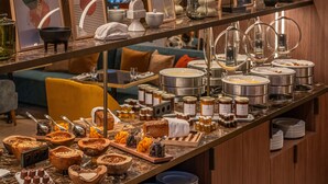 Disposição de buffet com diversos alimentos e acompanhamentos, incluindo potes de mel e recipientes com nozes.