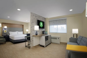 Quarto de hotel com cama, sofá, televisão, máquina de café e janela com persianas.