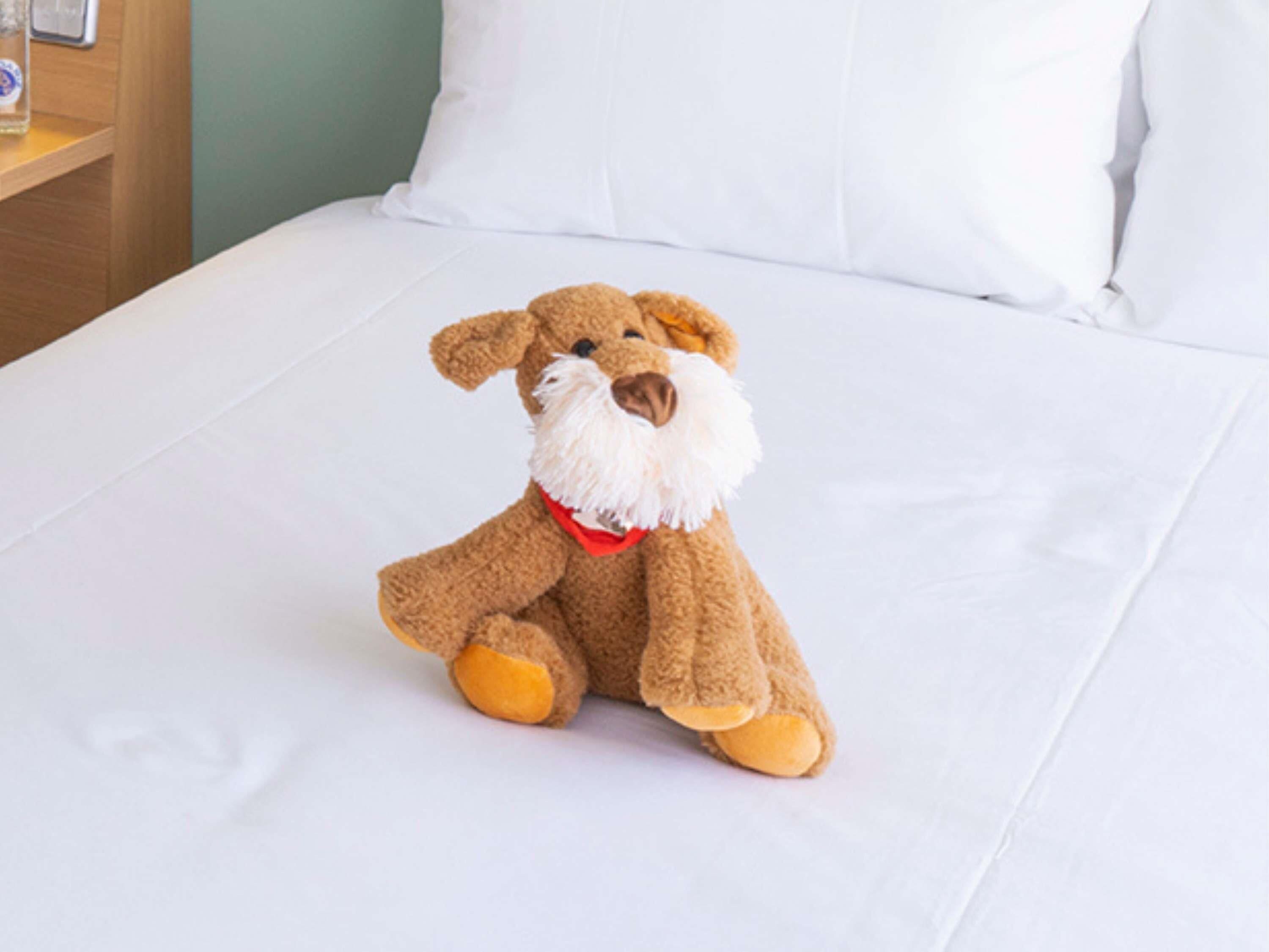 Um brinquedo macio sobre a cama, com roupa de cama branca.