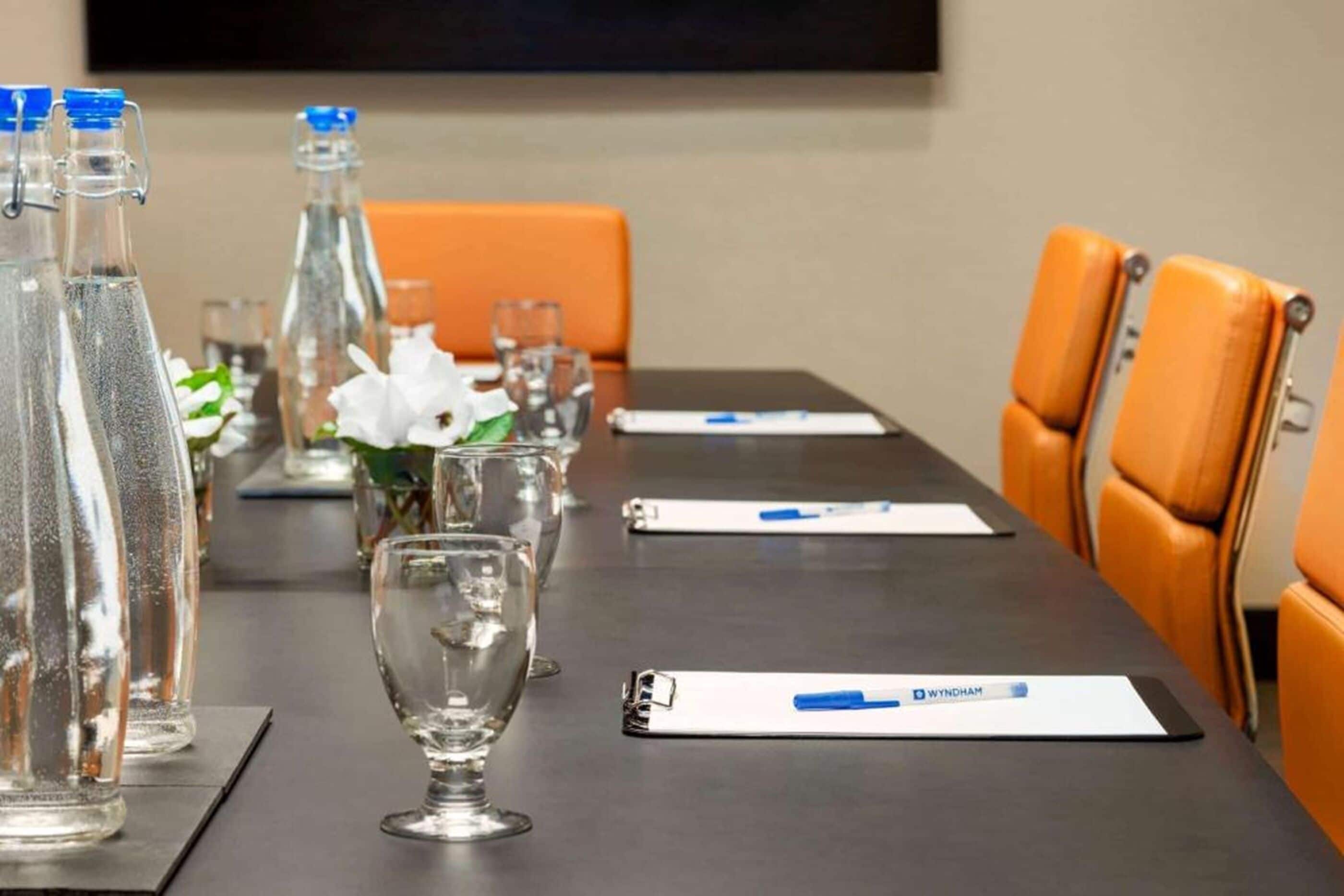 Uma mesa de conferência com garrafas de água, um copo e um arranjo floral branco.