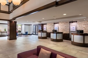 Um saguão de hotel com balcões de recepção, um sofá vermelho e uma parede de pedra.