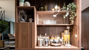 Um armário de madeira com prateleiras contendo utensílios de cozinha, uma cafeteira e um dispensador de suco.