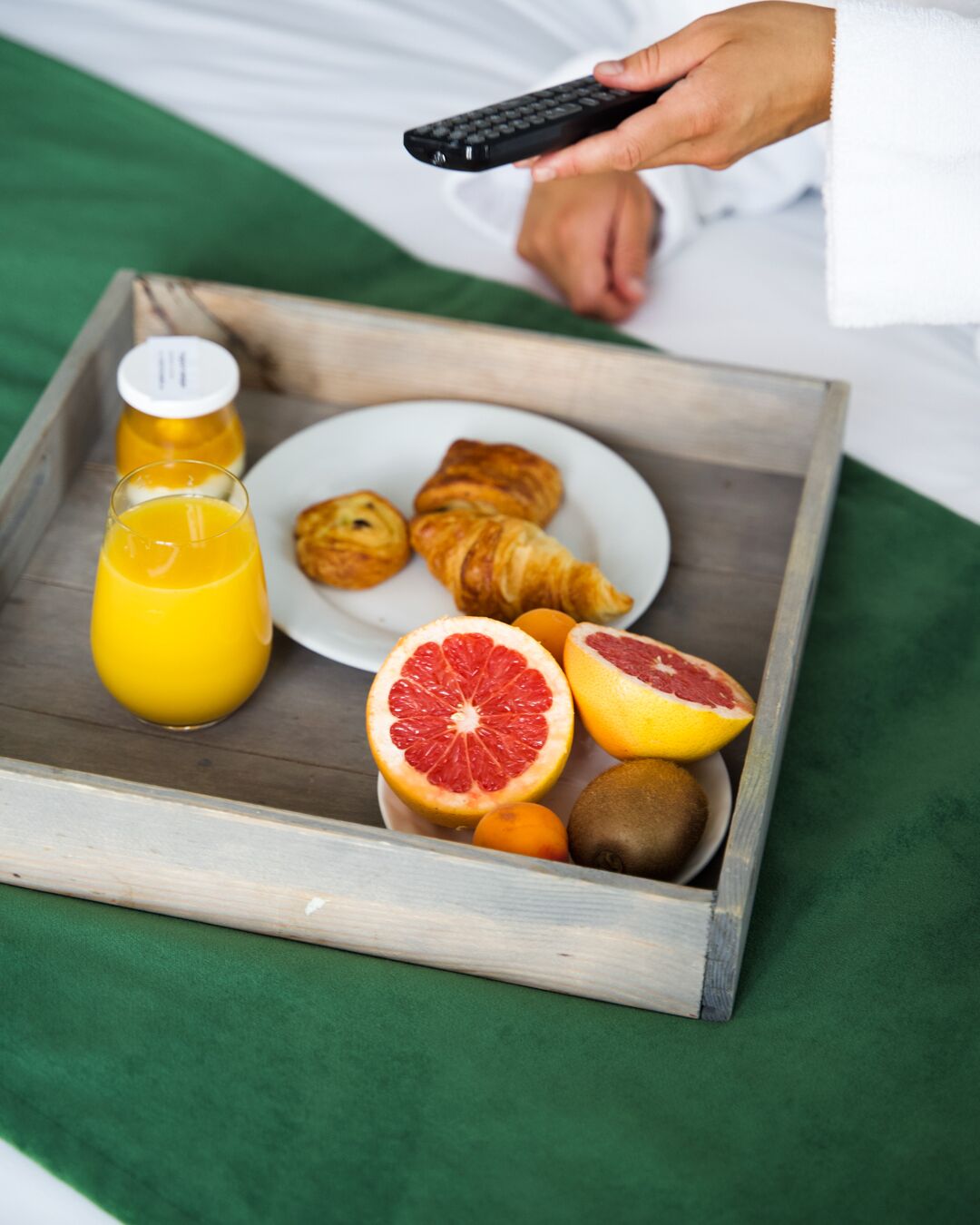 Uma bandeja com itens de café da manhã, incluindo croissants, toranja, kiwi, suco de laranja e uma garrafa de suco.