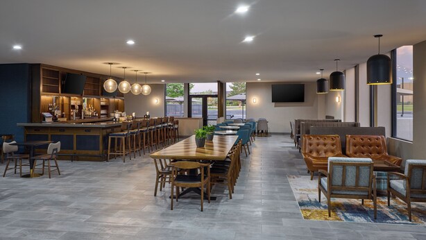 Uma sala de jantar espaçosa com uma mesa de madeira comprida, várias cadeiras, um bar e uma grande janela com vista.