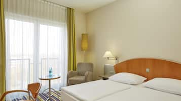 Quarto de hotel com duas camas, uma cadeira, uma mesinha e um abajur.