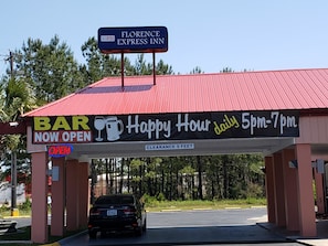 Um bar com telhado vermelho e uma placa indicando 'Happy Hour diário das 17h às 19h'.