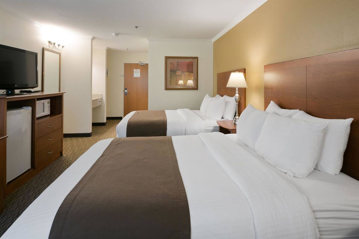 Quarto de hotel com duas camas, televisão, escrivaninha e abajur.