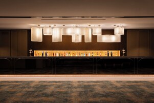 Área de bar com um balcão comprido, várias luminárias pendentes e uma seleção de garrafas.