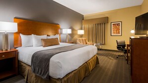 Quarto de hotel com uma cama grande, duas mesas de cabeceira com abajures, uma escrivaninha com cadeira, uma televisão e uma obra de arte emoldurada na parede.