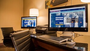 Quarto de hotel com escrivaninha, dois monitores, teclado e rato.
