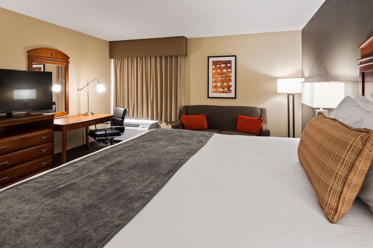 Quarto de hotel com cama, escrivaninha com computador, televisão, cadeira e abajur.